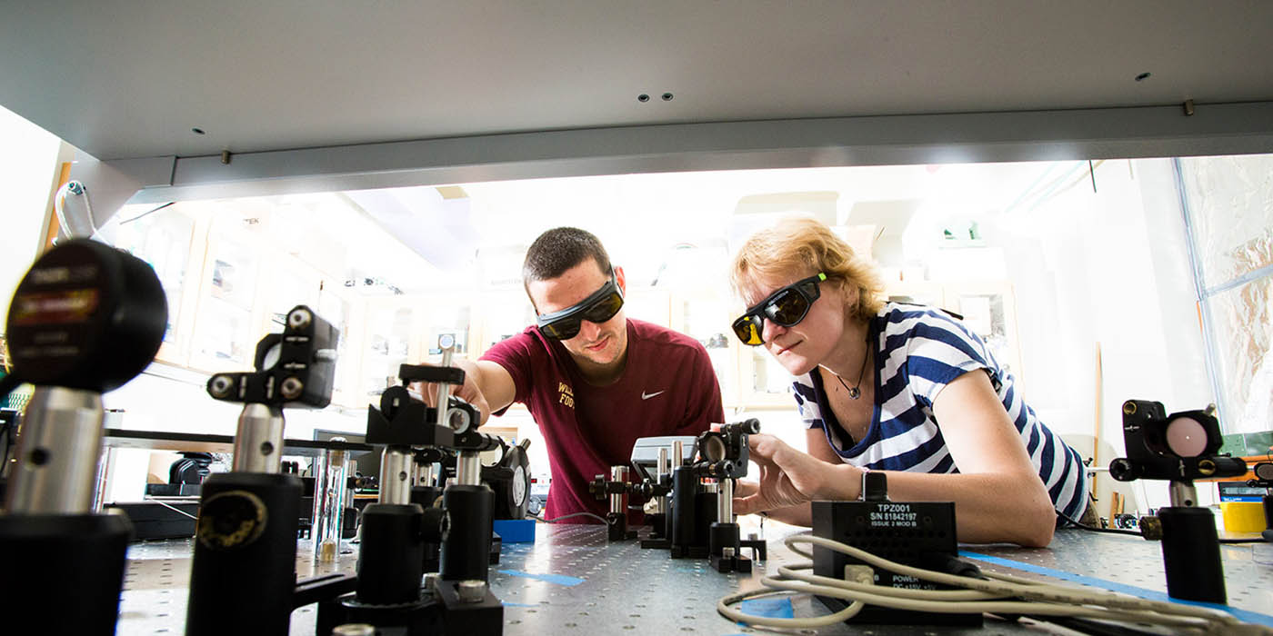 A physics professor and student, both wearing protective eyewear ...